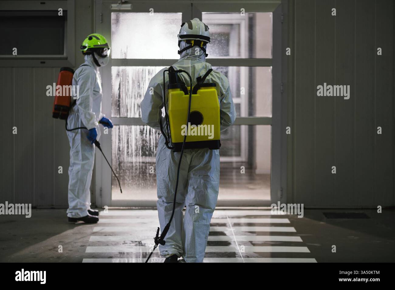 Hispanic firefighter in white PPE and respirators disinfects the ...