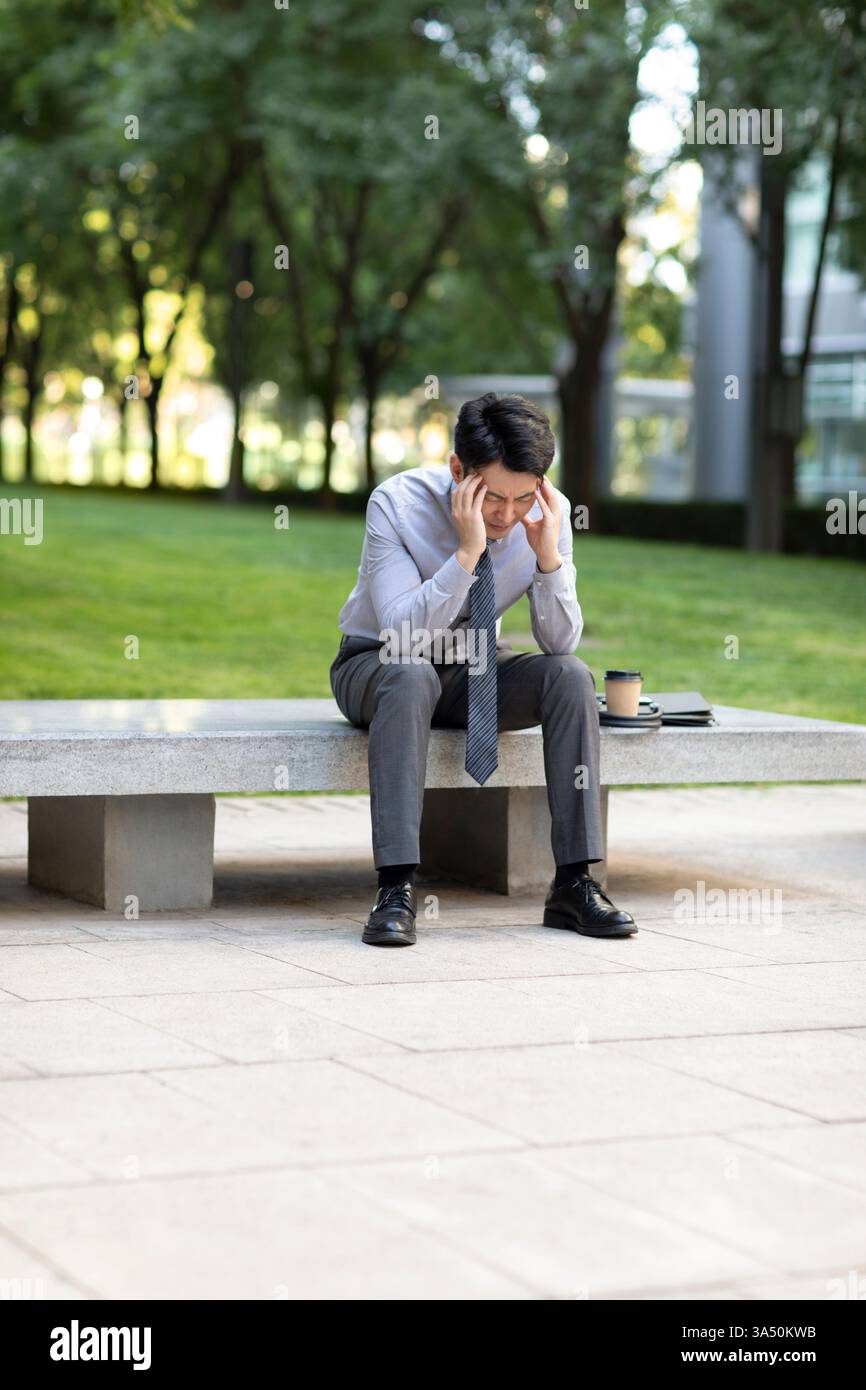 Chinese businessman leaning face on hands while sitting on bench in ...