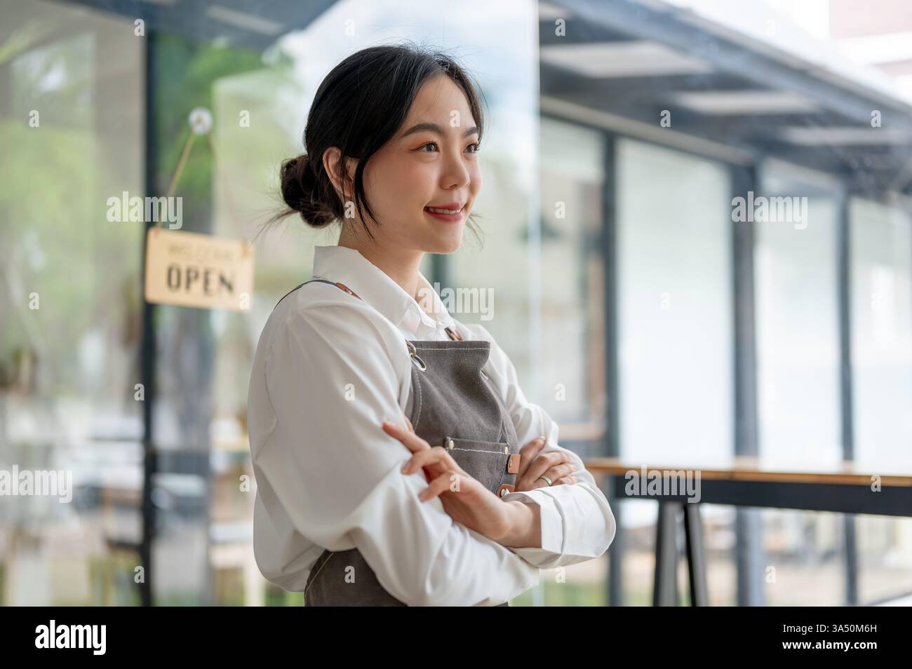 Smiling Asian business owner stands with arms crossed in her cafe. This ...
