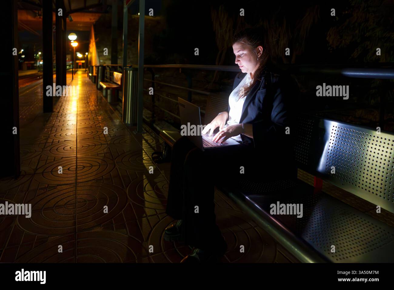 Woman in business attire working on laptop while waiting for train at ...