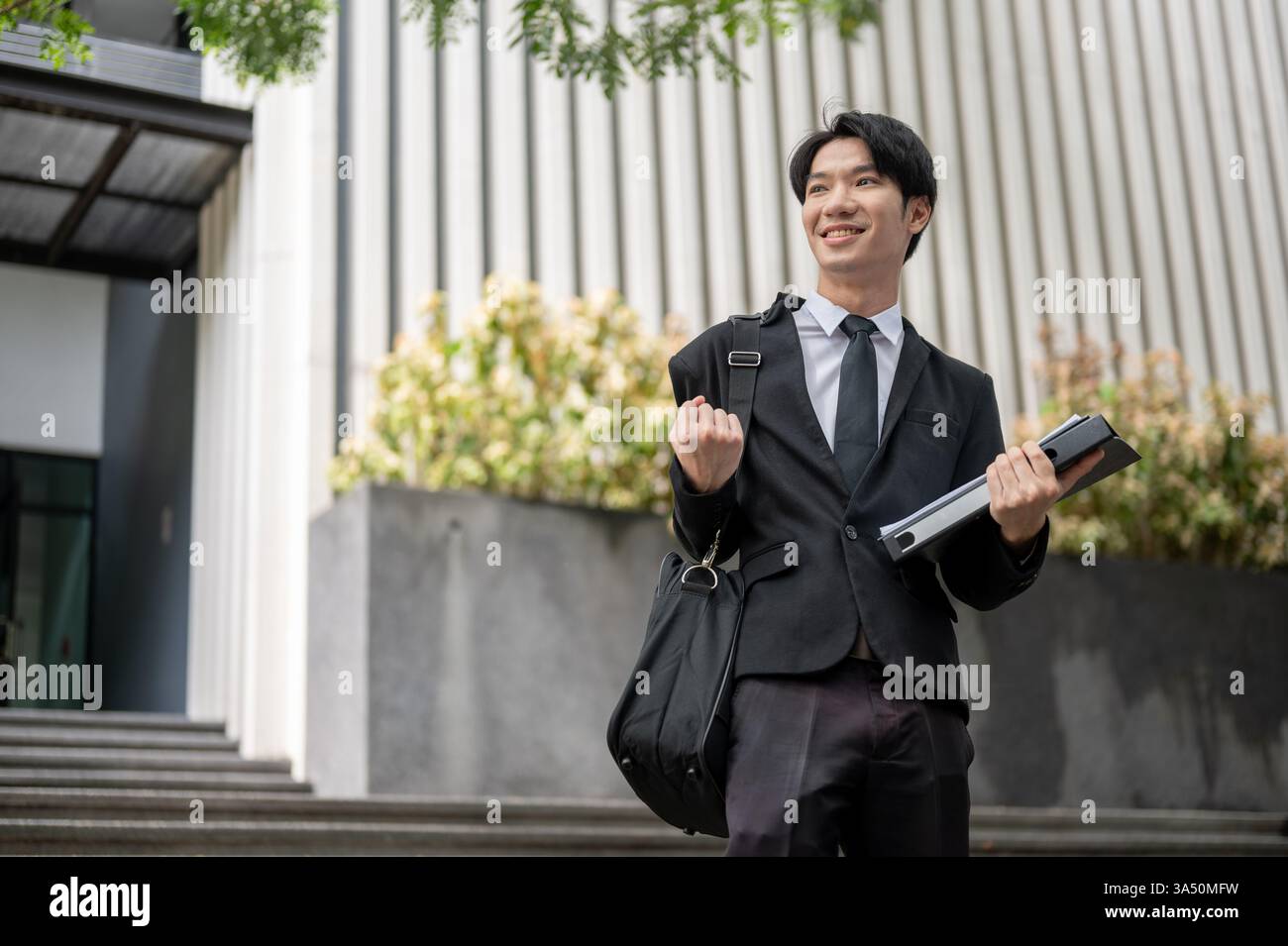 Smiling Asian businessman holding binder and raising clenched fist ...