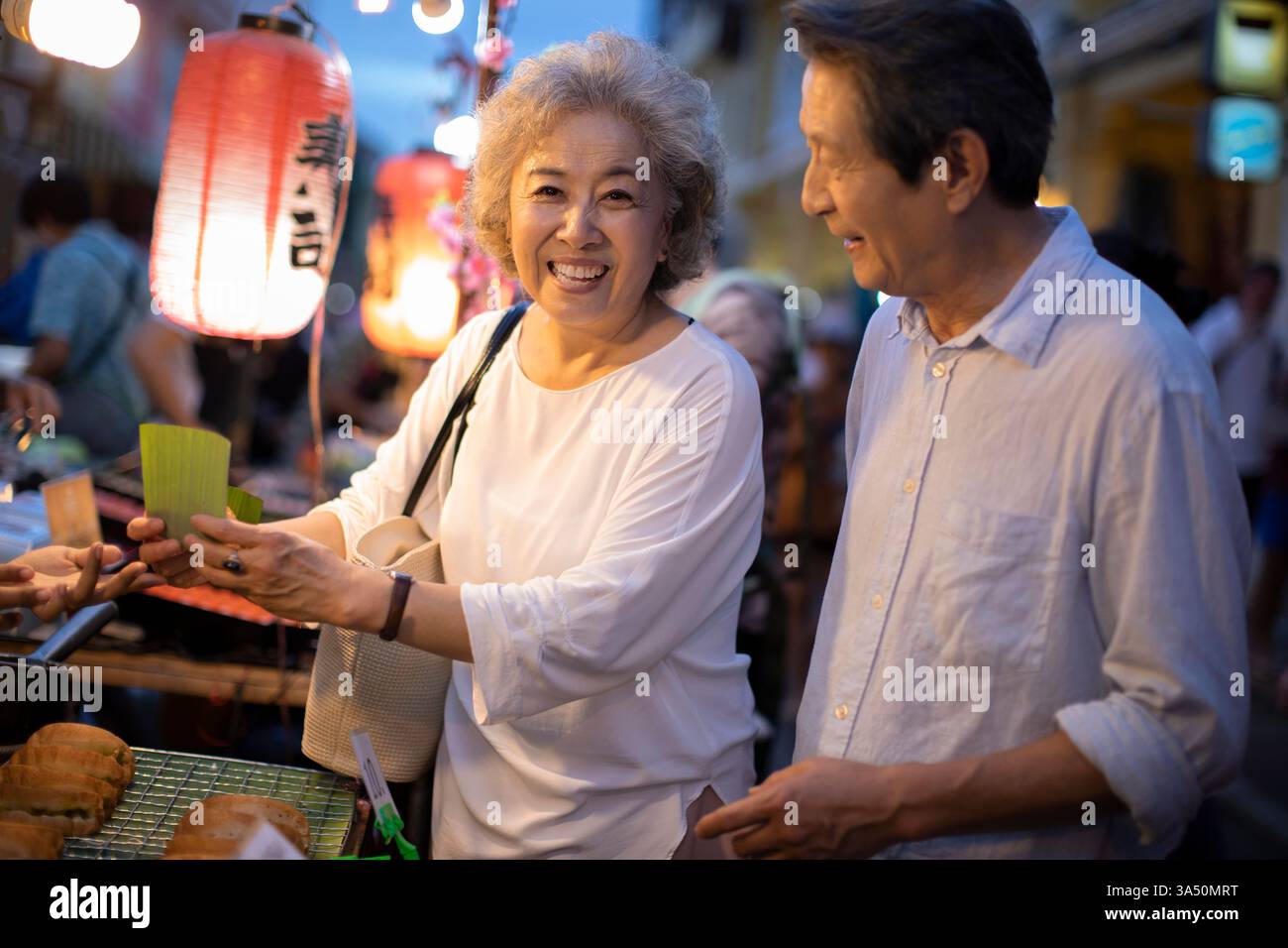 Smiling senior Chinese couple buying street foods while standing ...