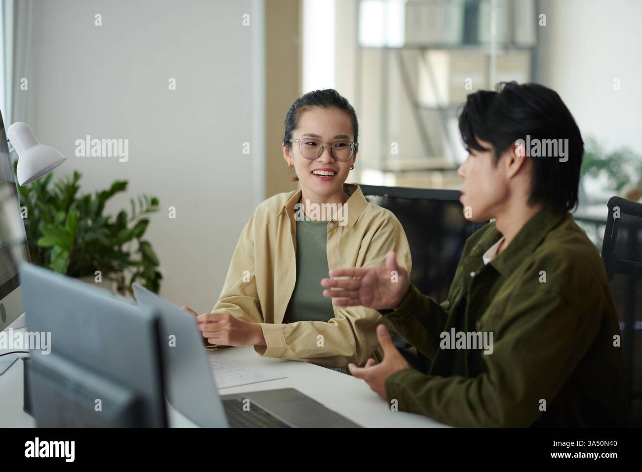 Asian female programmer wearing eyeglasses discussing project details ...