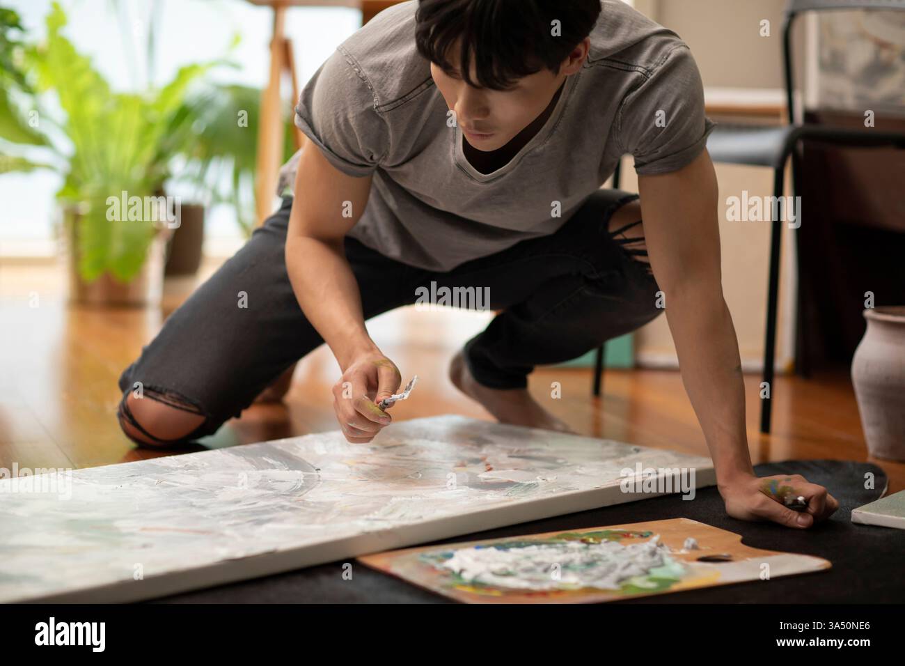 Chinese man painting on canvas while crouching on the floor at home ...
