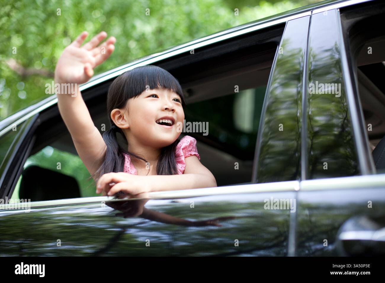 Smiling Chinese girl waving out of car window during travel Stock Photo ...