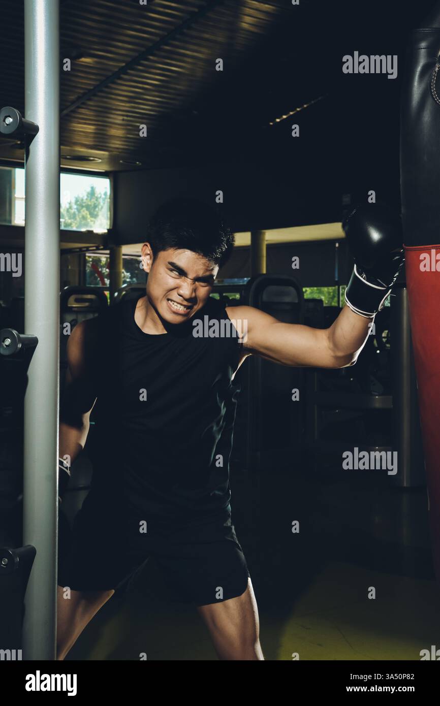 Asian male boxer training in a gym, delivering punches to a hanging bag ...