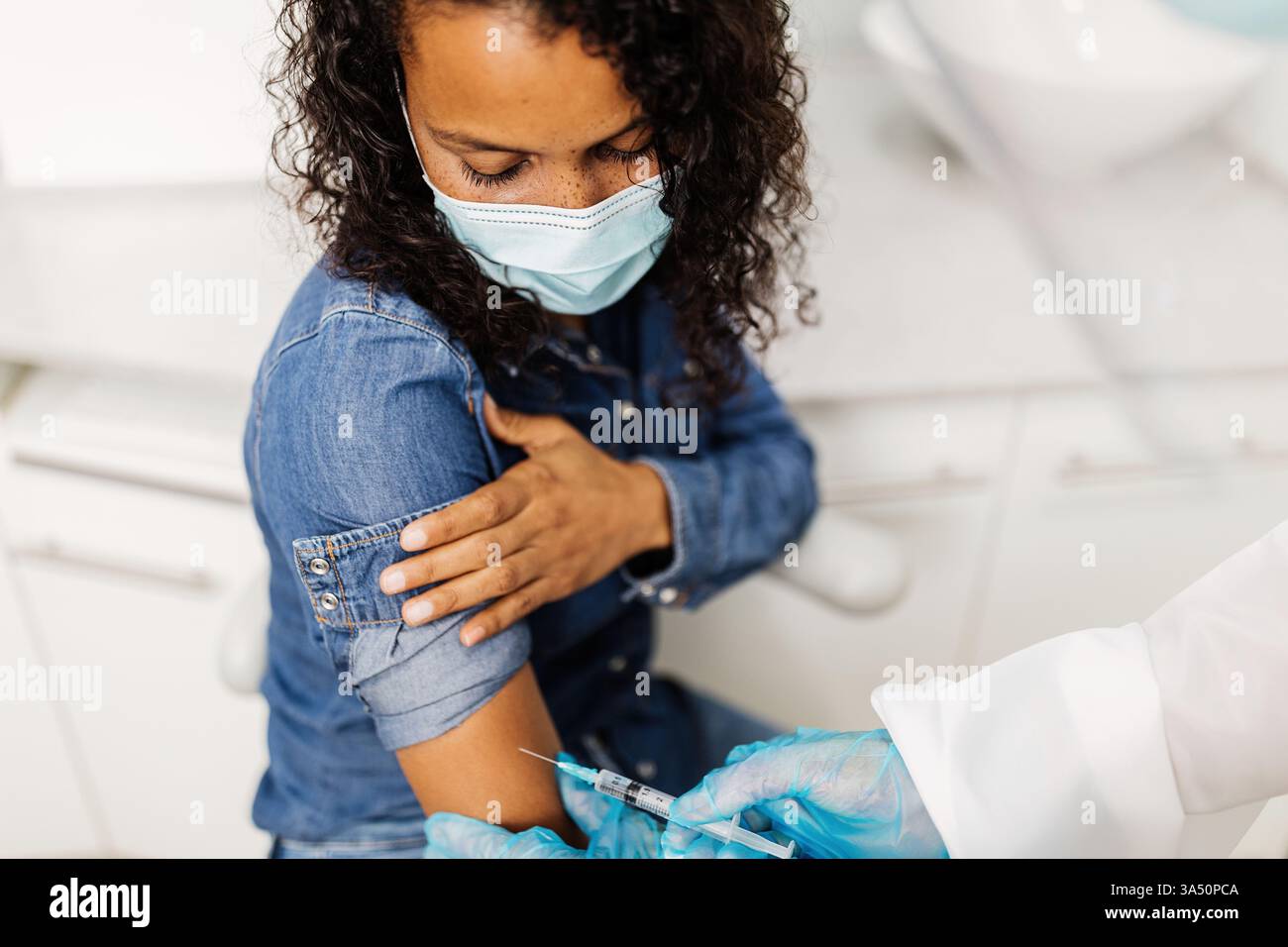 Black woman wearing a face mask receives a vaccination from a doctor in ...