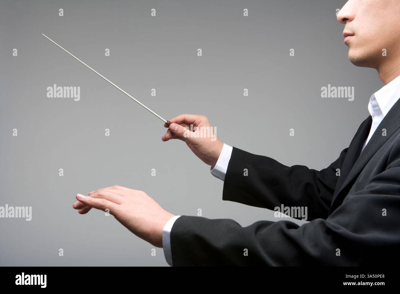 Portrait of a Chinese male conductor directing with a baton in a studio ...