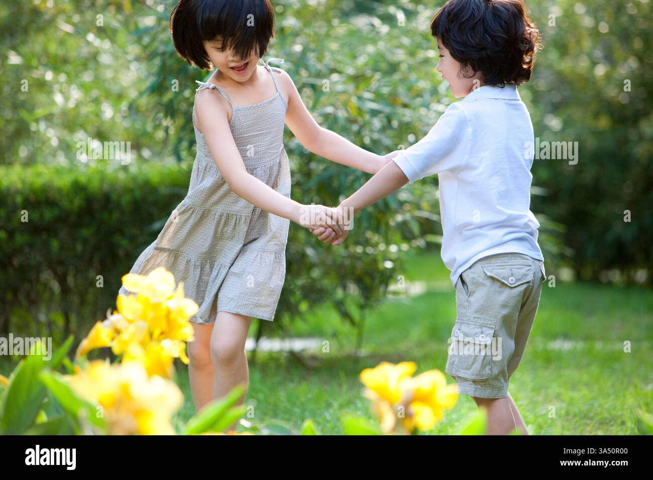 Two Chinese children play happily in a garden on a sunny day. The scene ...