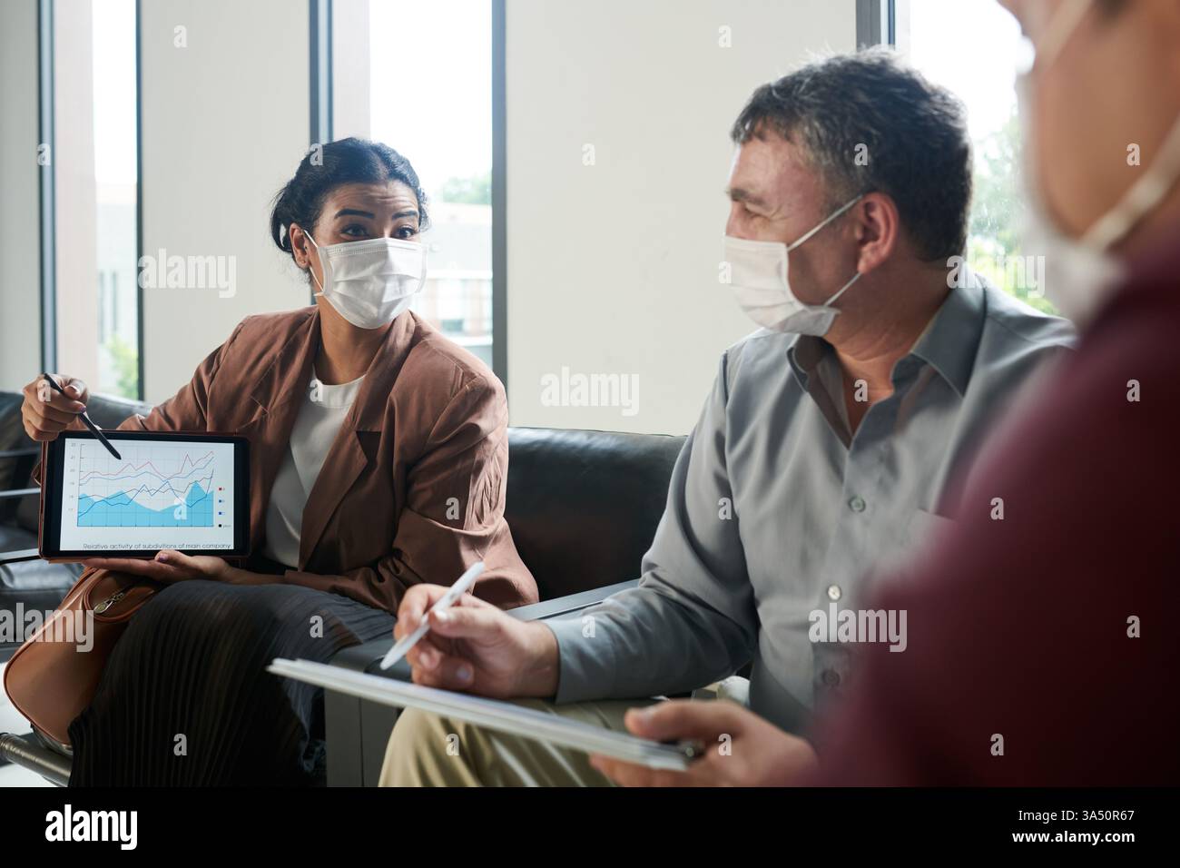 Mixed race woman wearing facemask holding tablet discussing progress ...