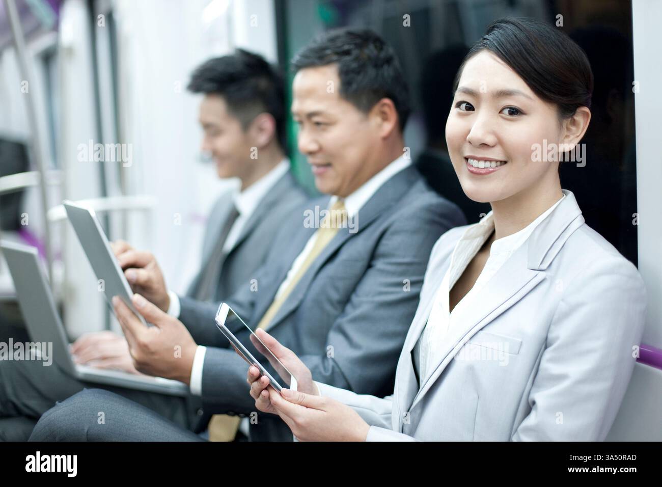 Chinese businesswoman with colleagues using gadgets on a subway train ...