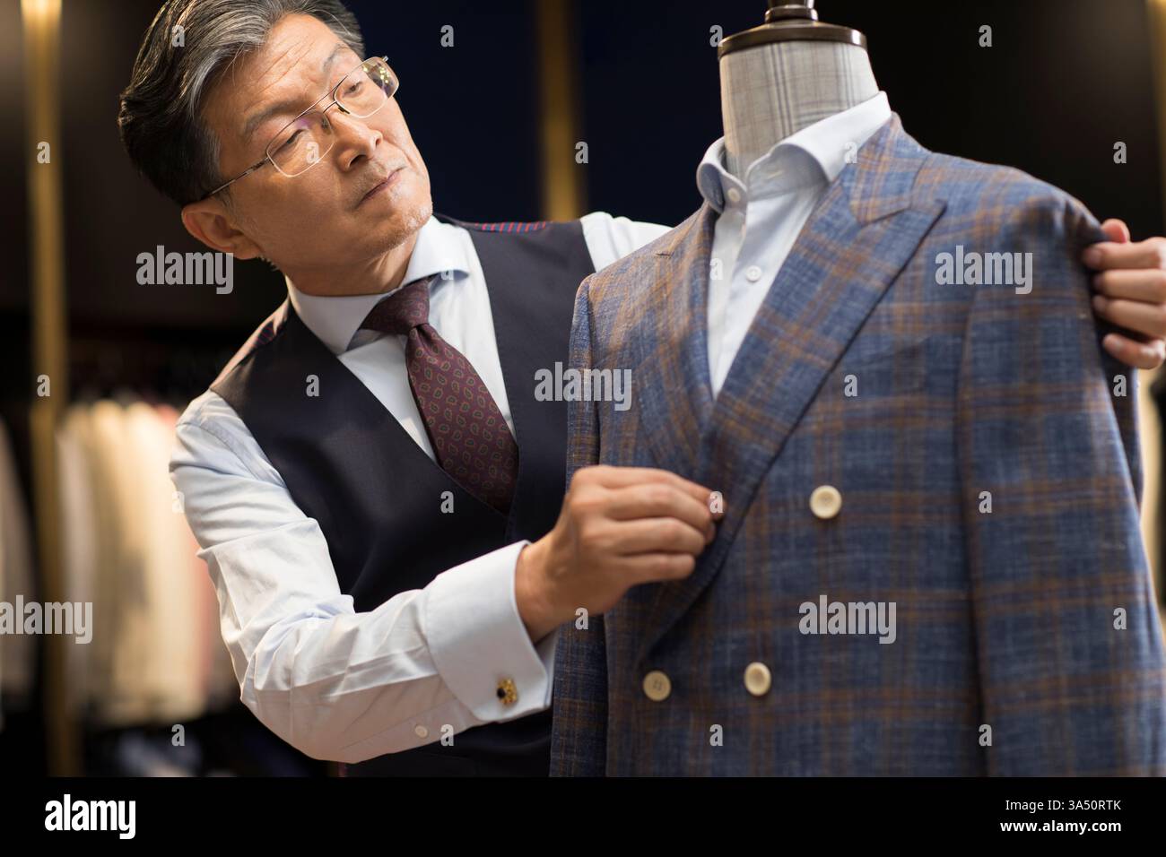 Senior Chinese male fashion designer standing and making adjustments on ...