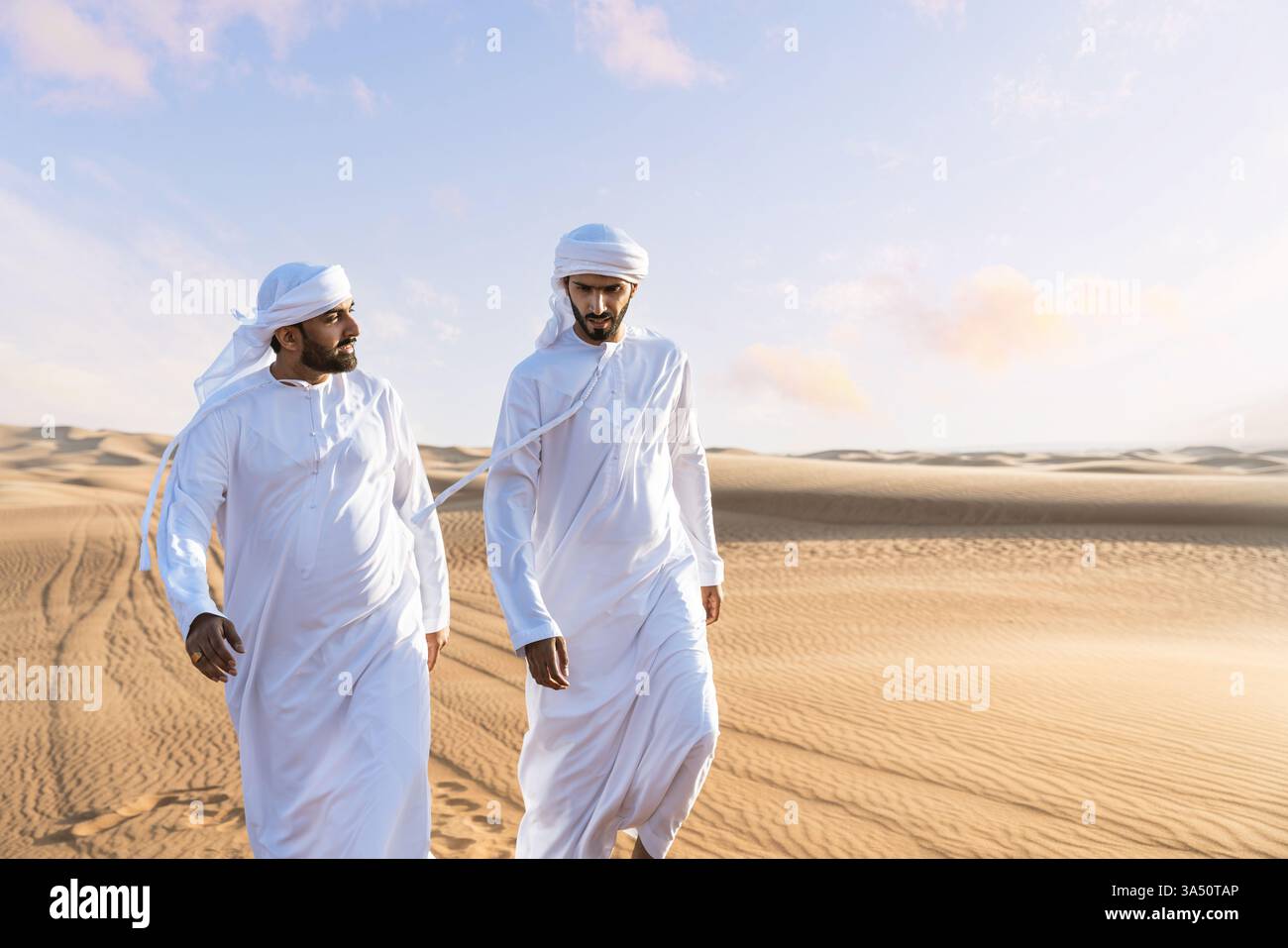 Two Middle Eastern men in kanduras bond in the desert near Dubai's sand ...