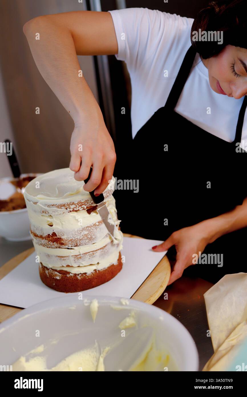 A person skillfully applies frosting to a multi-layer cake, assembling ...
