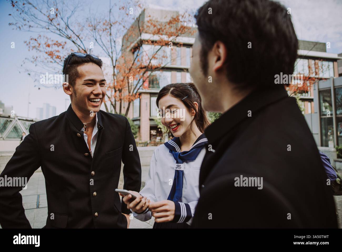 Cheerful Asian female student having fun using smartphone standing with ...