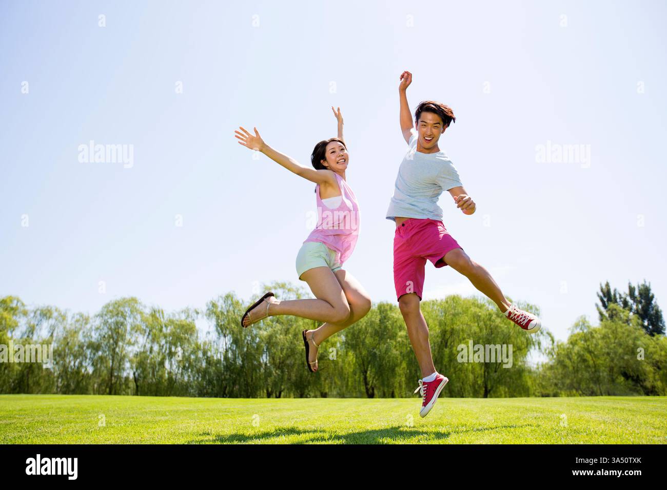 Cheerful young Chinese man and young woman jumping on grass Stock Photo ...