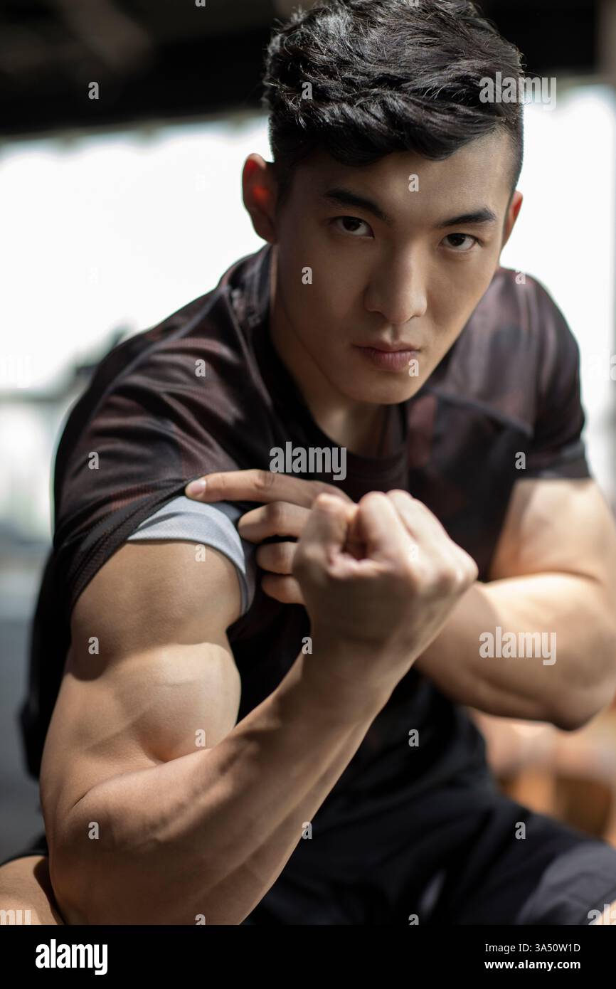 Chinese man flexing his arm muscle while sitting on workout bench in ...