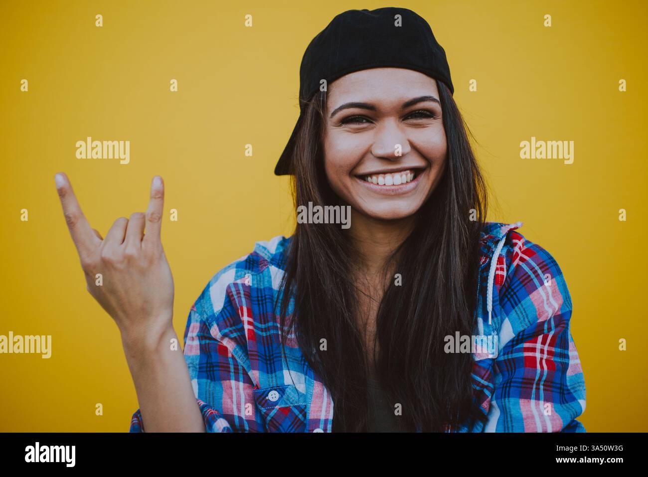 Smiling Hispanic woman wearing cap showing rock and roll hand gestures ...