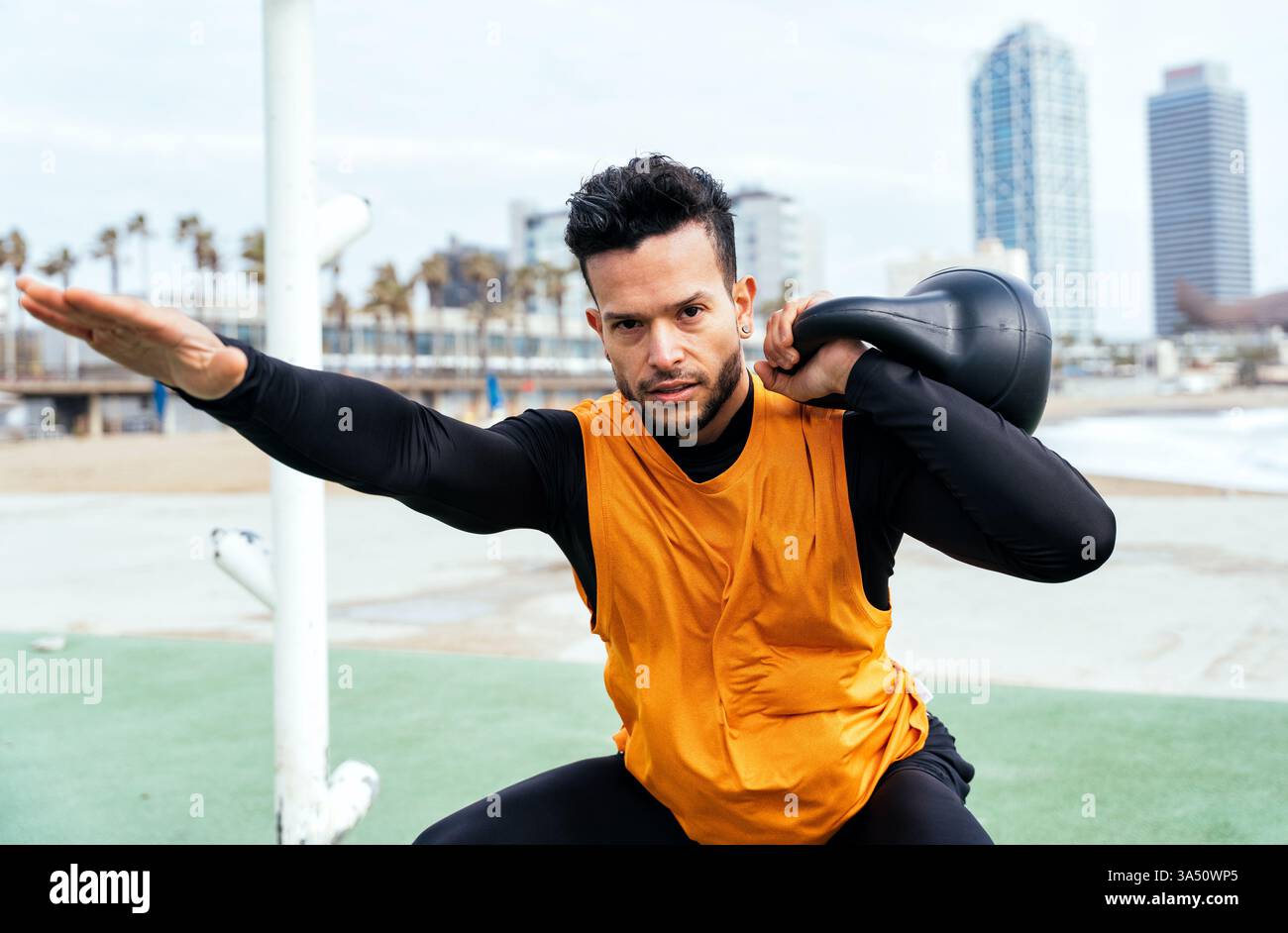 Hispanic male crouching with arm raised holding kettlebell while doing ...
