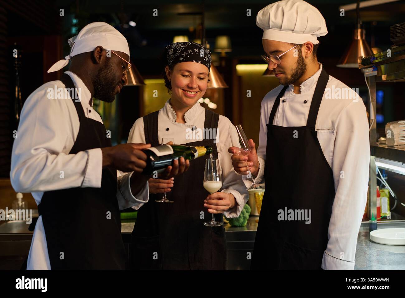 Young African American male chef pouring champagne into flutes held by ...