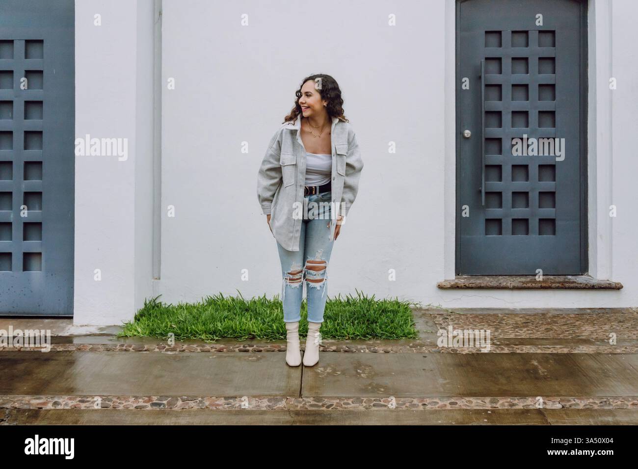 Hispanic woman looking sideways standing between two doors during rainy ...