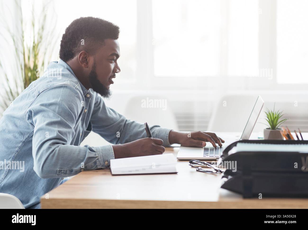 Young African American employee using laptop and taking notes while ...