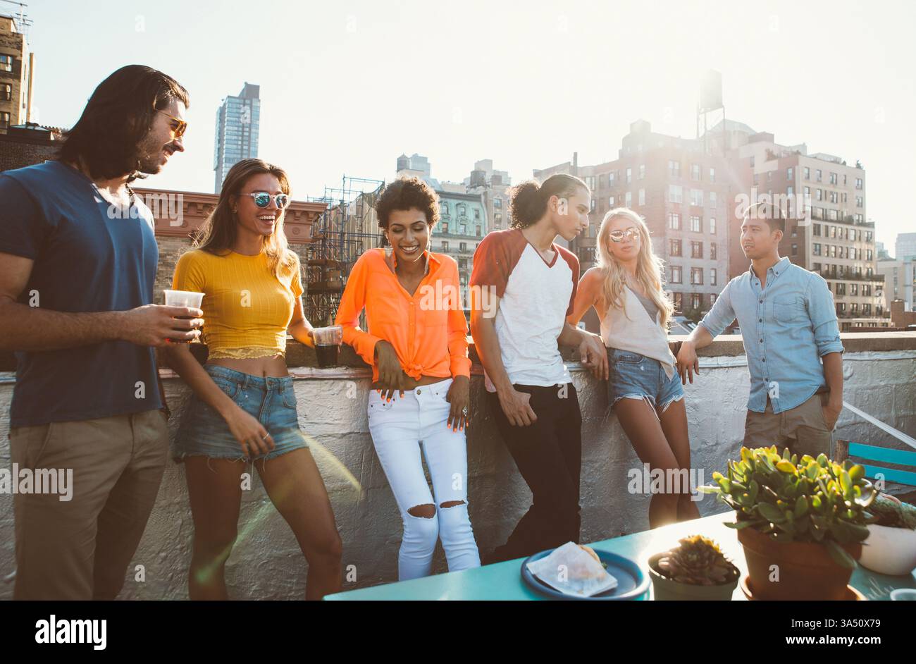 Group of diverse male and female friends standing leaning on rooftop ...