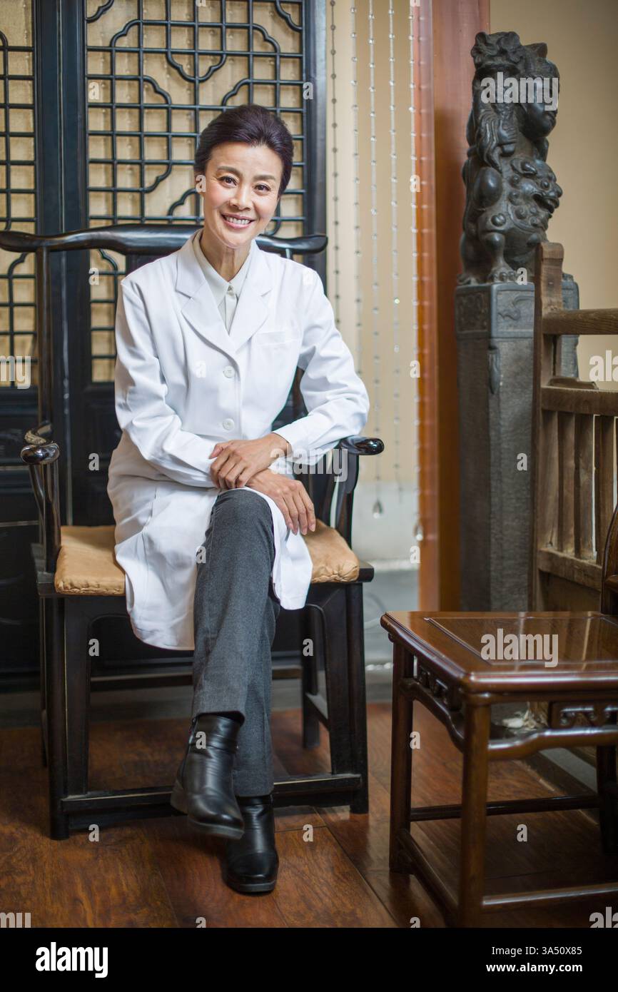 Portrait of a Chinese female doctor indoors, seated with a lab coat and ...