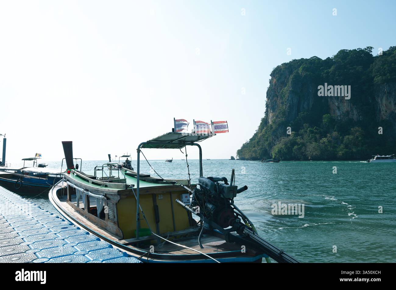 A traditional long-tail boat with tattered Thai flags docked at a ...