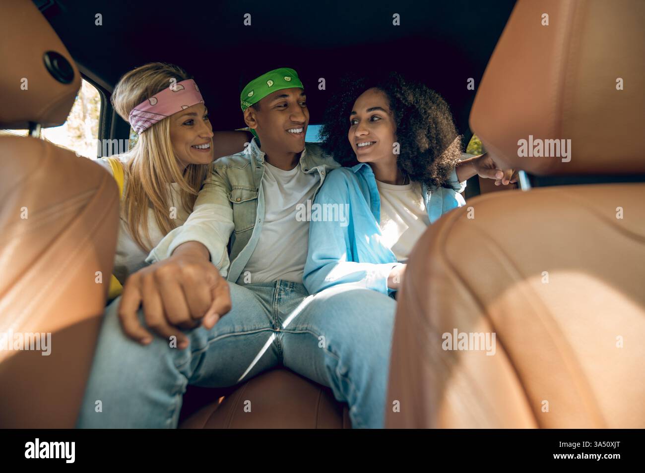 Smiling Black man sitting on back seat of a car with female friends ...