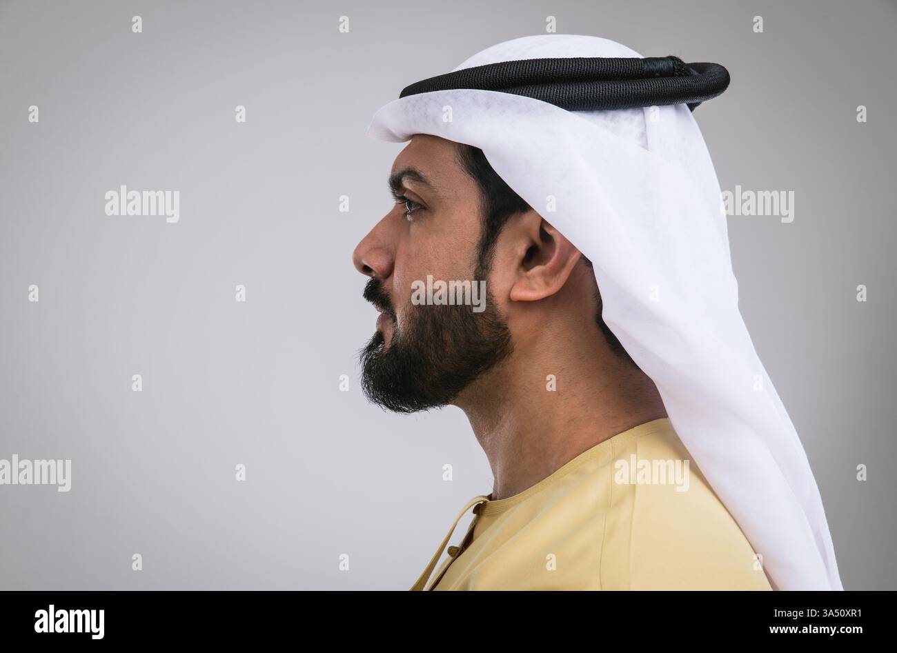 Serious Middle Eastern man looking away standing sideways against gray ...