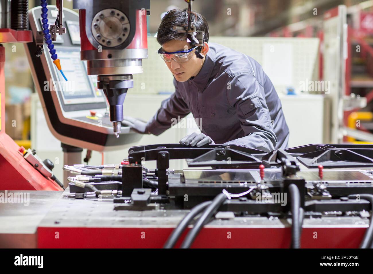 Chinese male mechanical engineer in safety glasses operating a machine ...