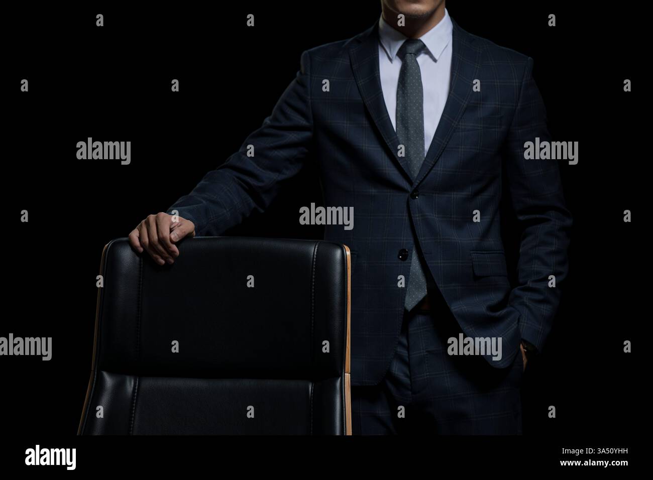 Chinese businessman with hand in pocket standing behind chair in dark ...