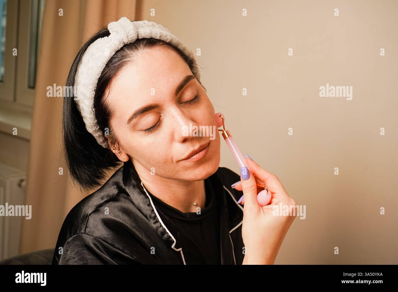 The lighting creates a peaceful mood. Using a facial roller, a woman ...