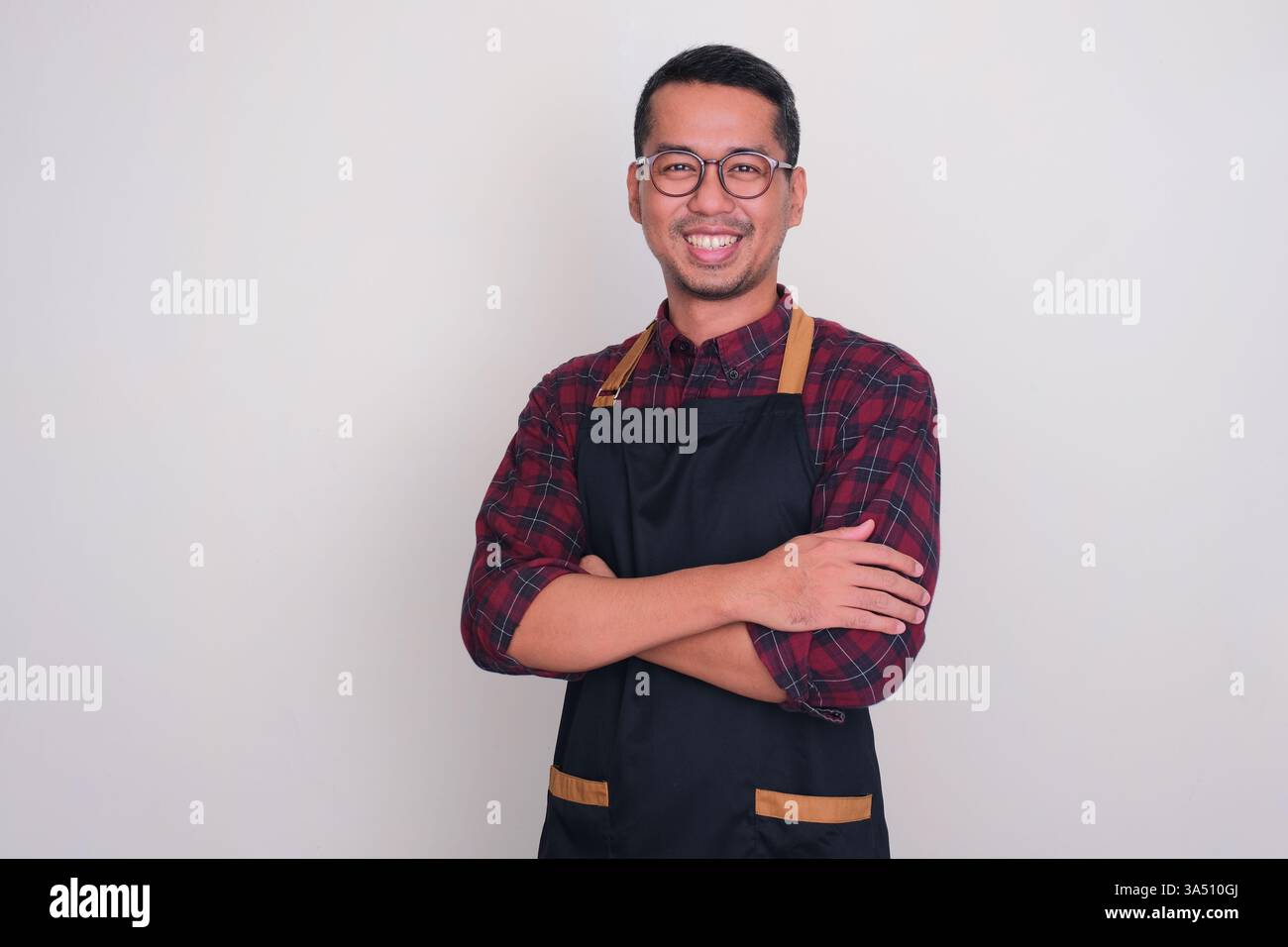 A man wearing an apron smiles confidently with arms crossed in a cafe ...