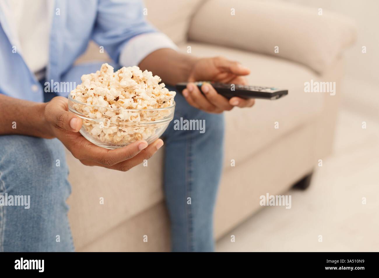 African american guy watching TV at home, holding tv remote controller and popcorn in hands ...