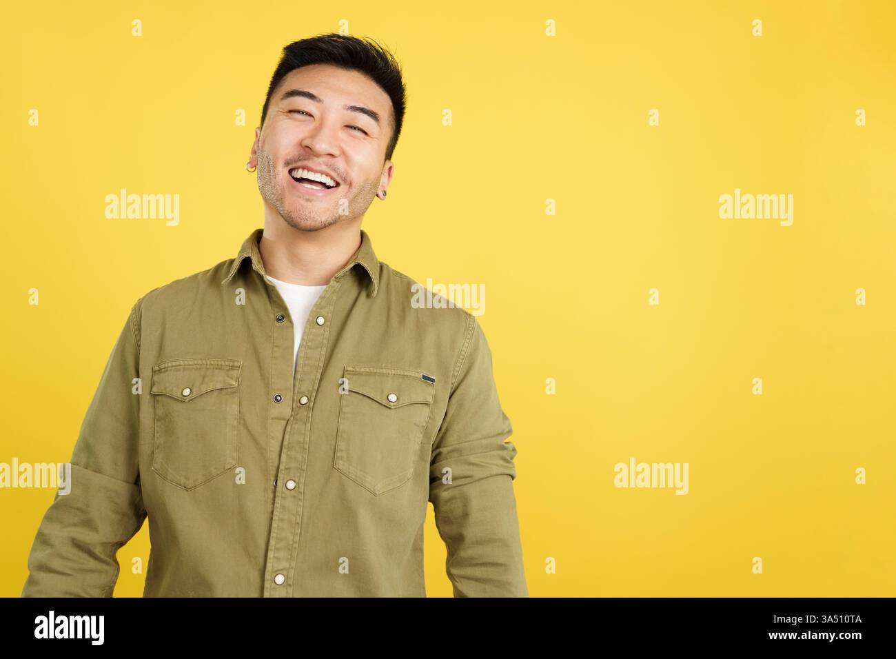 Smiling Asian man laughing while standing against yellow background ...