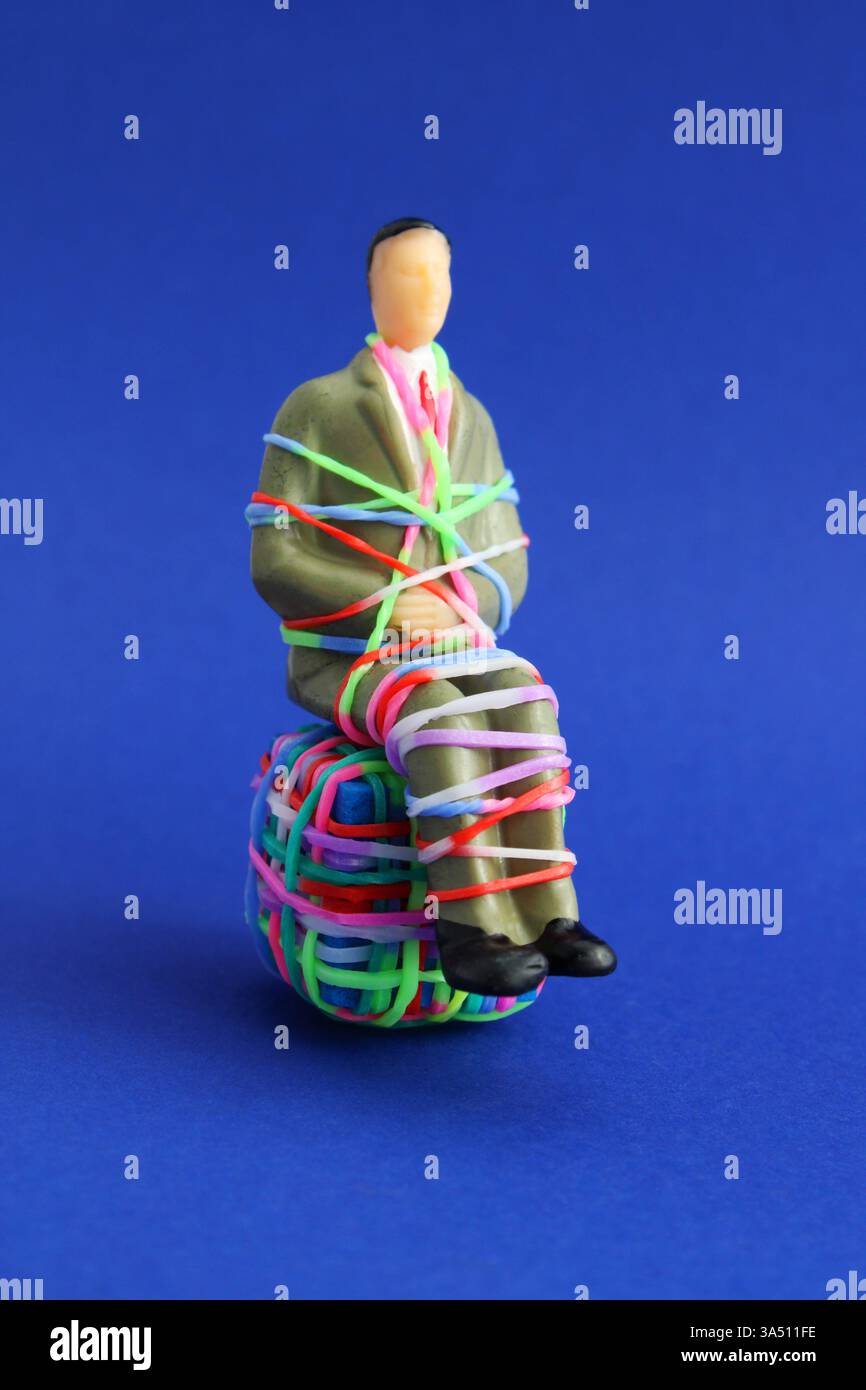 Executive tied with rubber bands sitting on a cube Stock Photo - Alamy