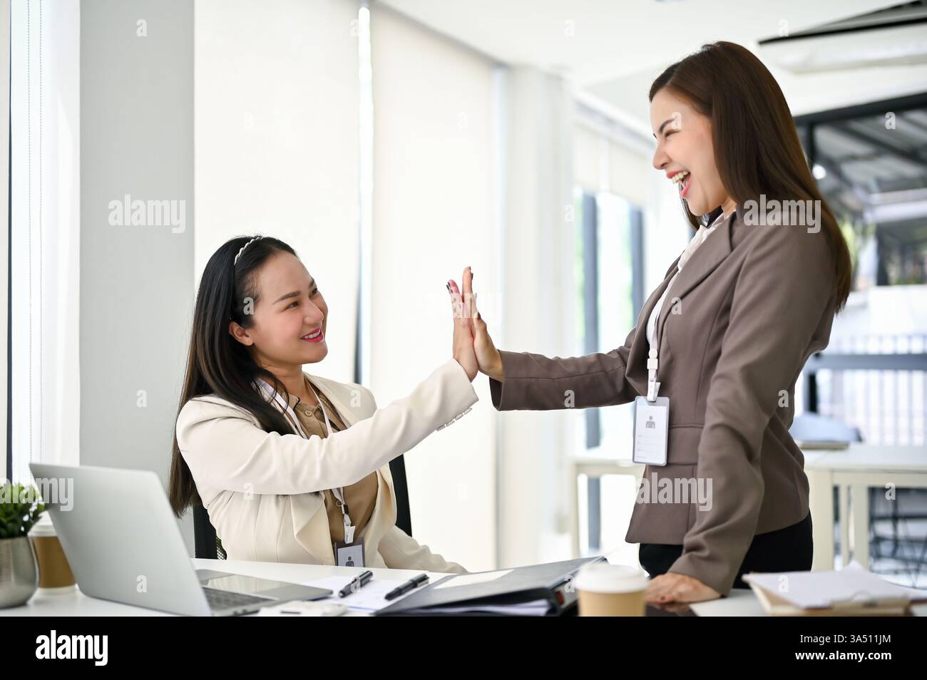 Two cheerful and happy millennial Asian businesswomen are giving high ...
