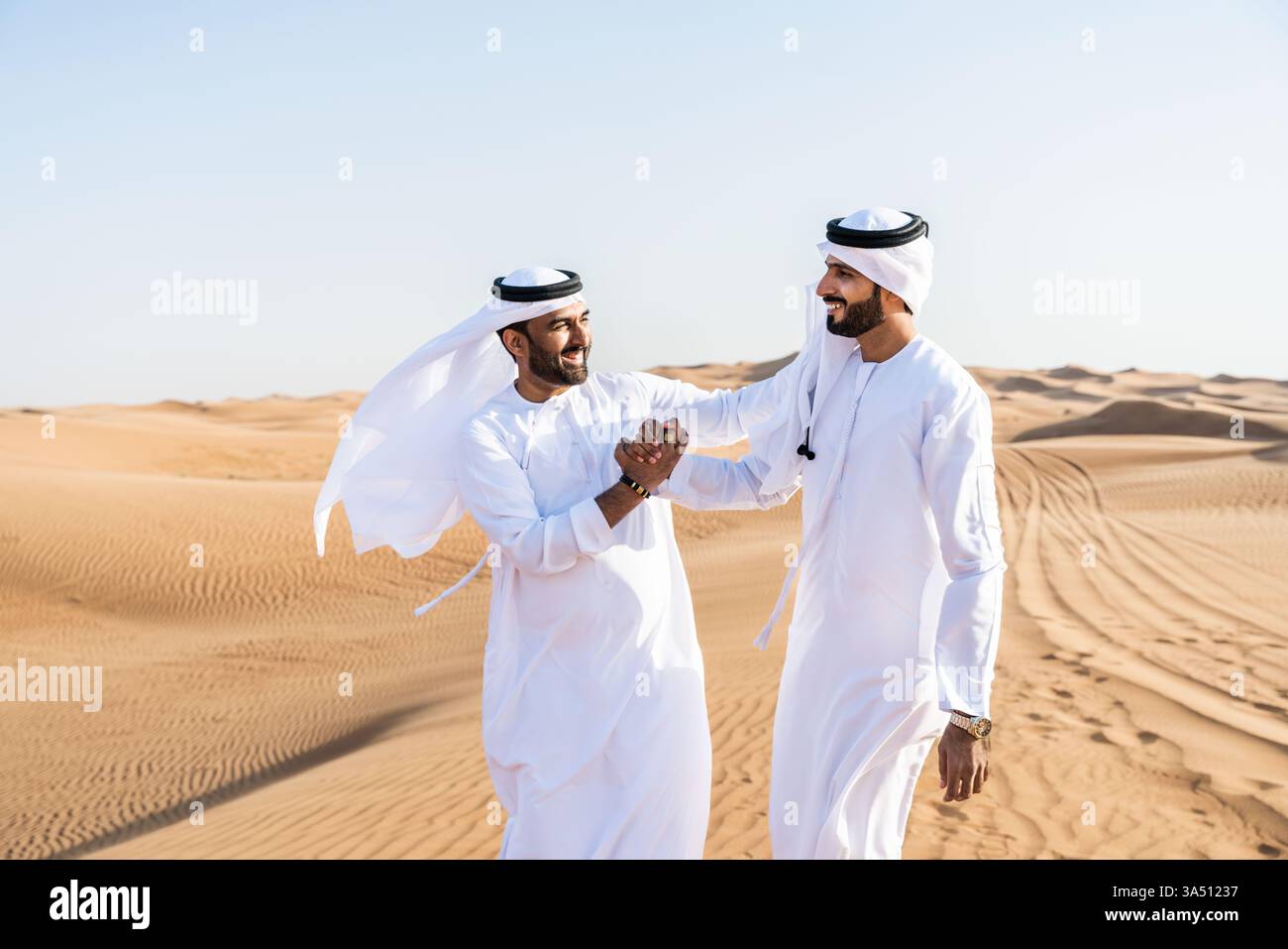 Two middle-eastern men wearing traditional emirati arab kandura bonding ...