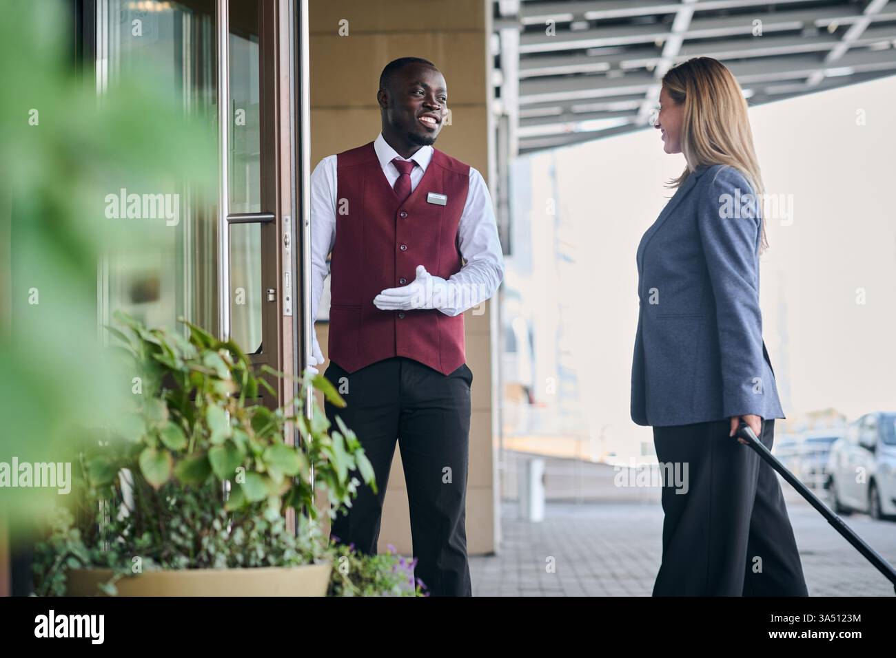 Black bellboy welcoming caucasian female guest with luggage while ...