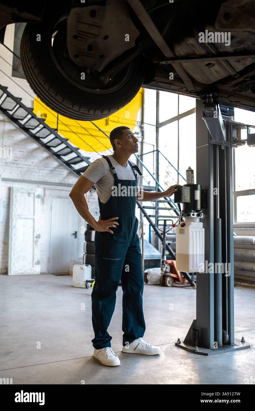 African American male mechanic using car lift while doing inspection in ...