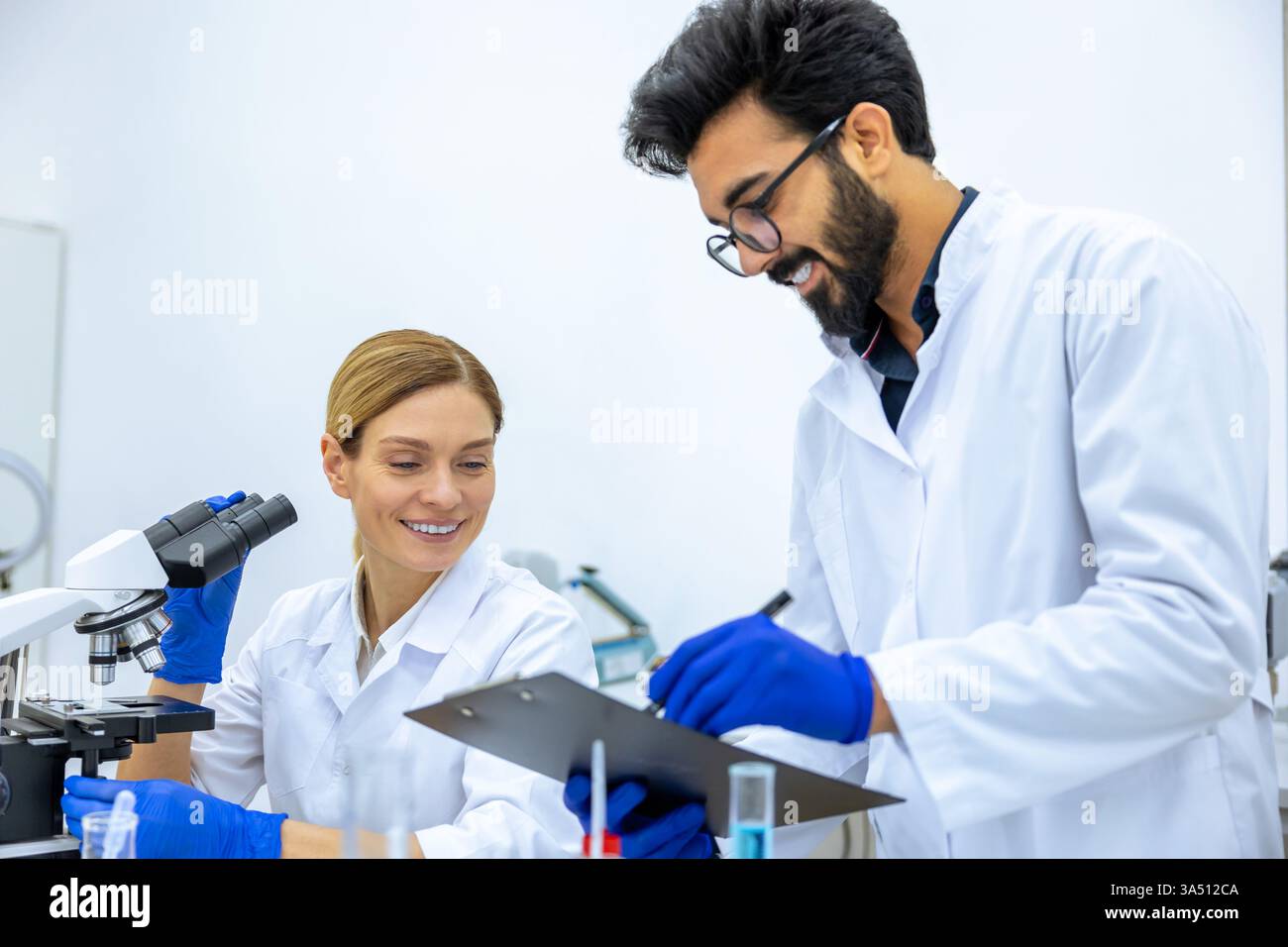 Cheerful Indian male scientist wearing lab coat and latex gloves making ...