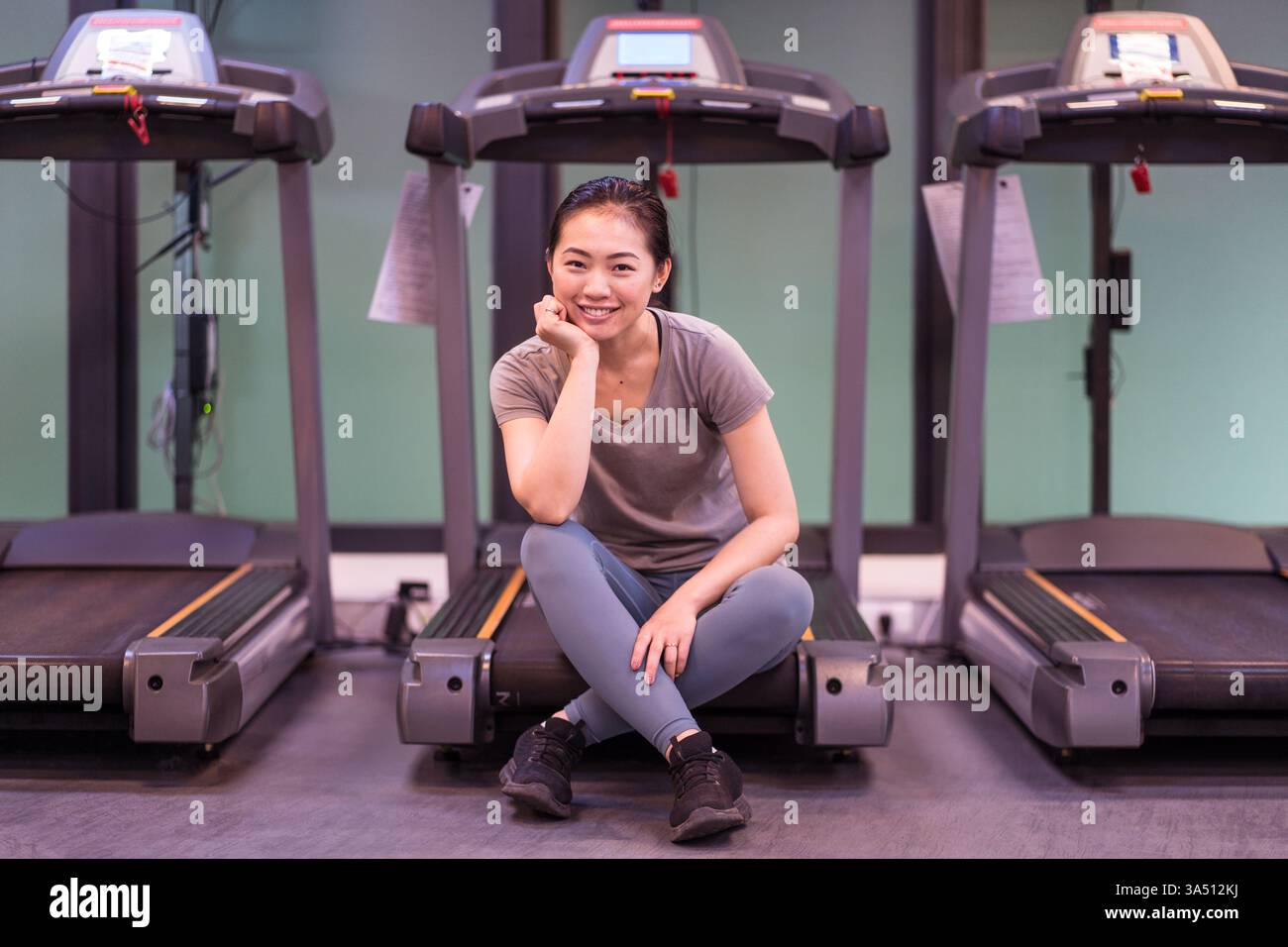Asian woman athlete in active wear resting sitting on treadmill after ...