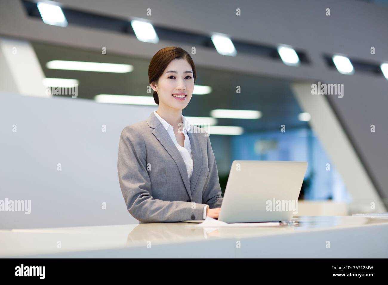 Smiling Chinese female receptionist stands at the front desk with a ...