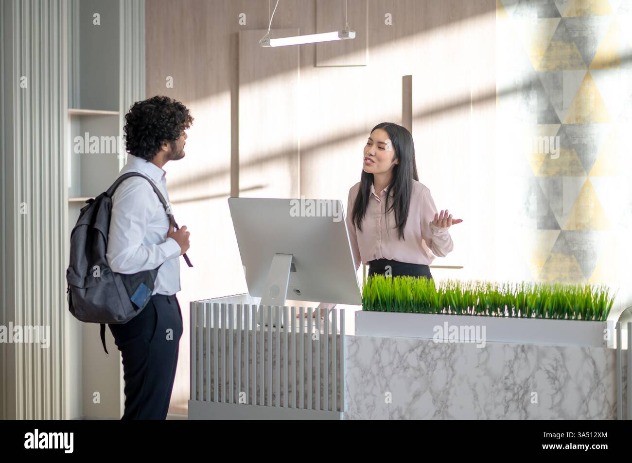 Indian male with curly hair carrying backpack talking to Asian female ...