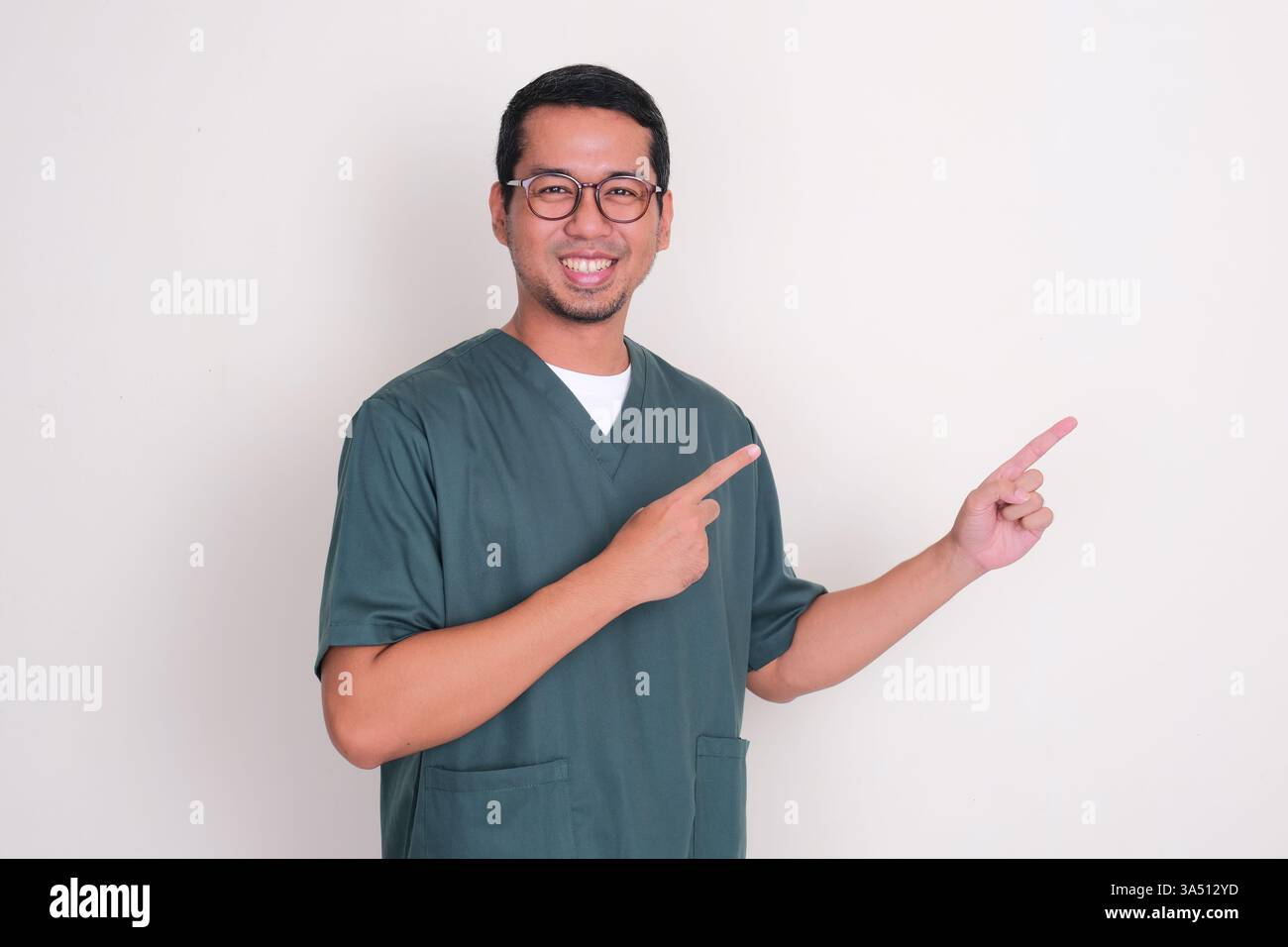 Smiling Asian nurse poses with a friendly pointing gesture against a ...