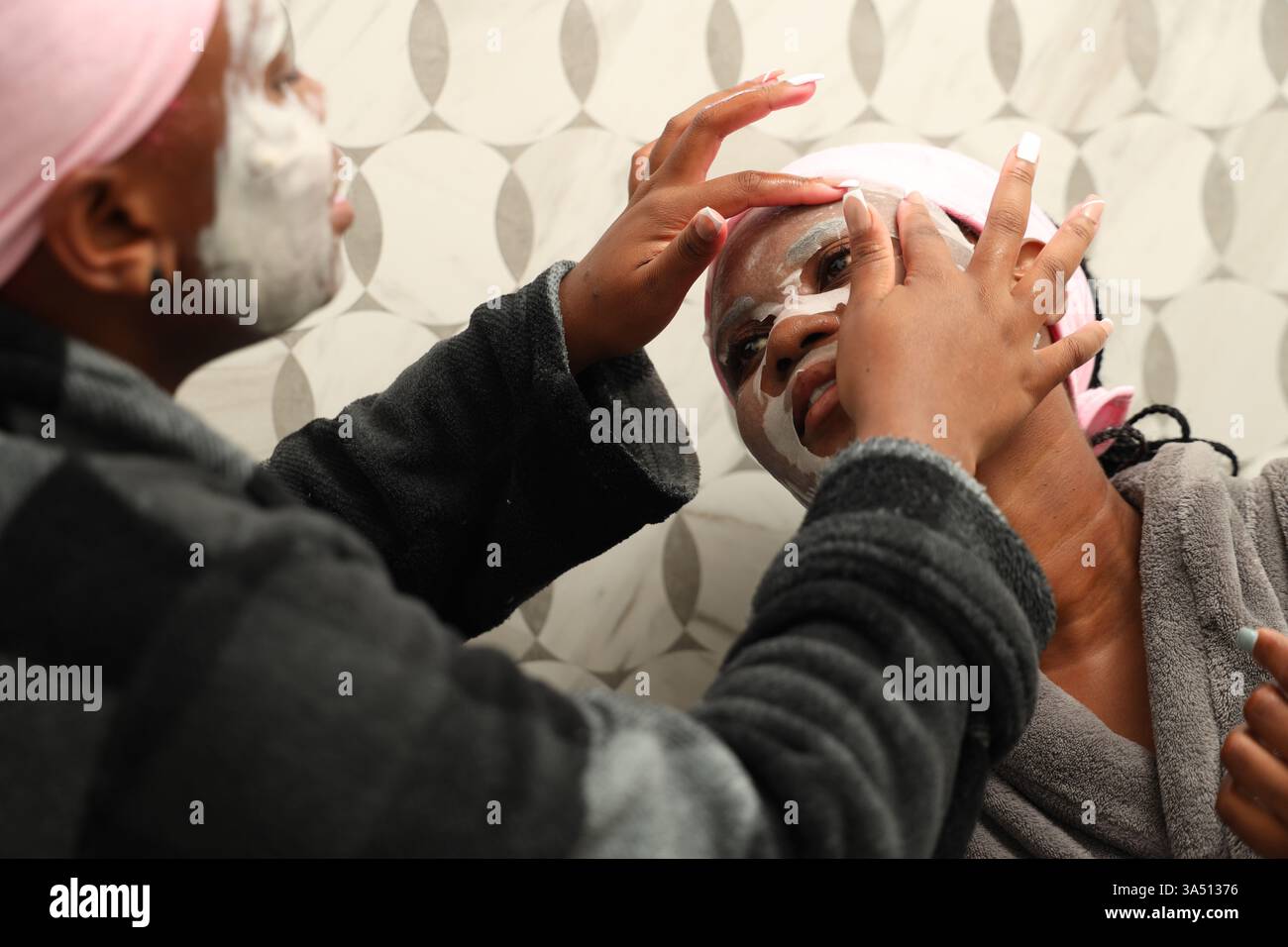 Black teen female helping Black woman friend fixing face mask in ...