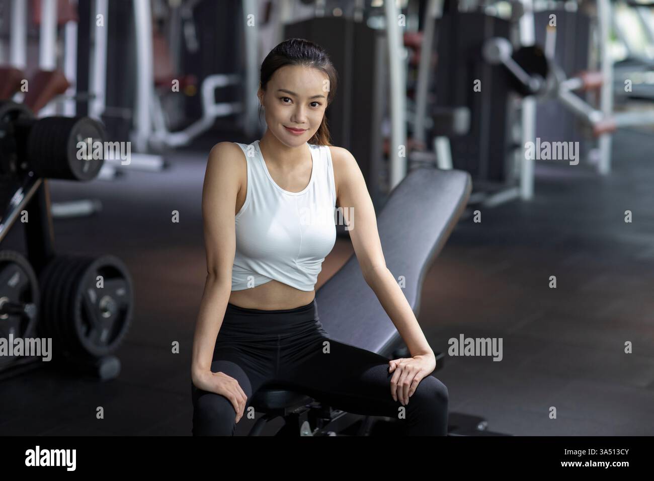 Smiling Chinese woman sitting on workout bench in gym Stock Photo - Alamy
