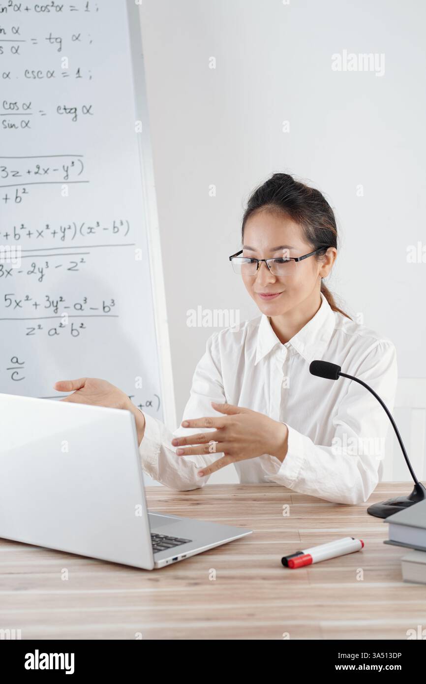 Smiling Asian female math teacher explaining difficult topic to student ...